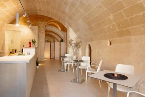 Um interior moderno com um arco de pedra, uma mesa de recepção e cadeiras brancas ao redor de uma mesa.
