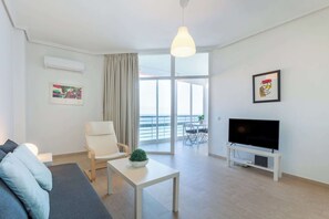 Uma sala de estar moderna com um sofá, uma poltrona, uma mesa de centro, uma televisão em um suporte e uma varanda com vista.