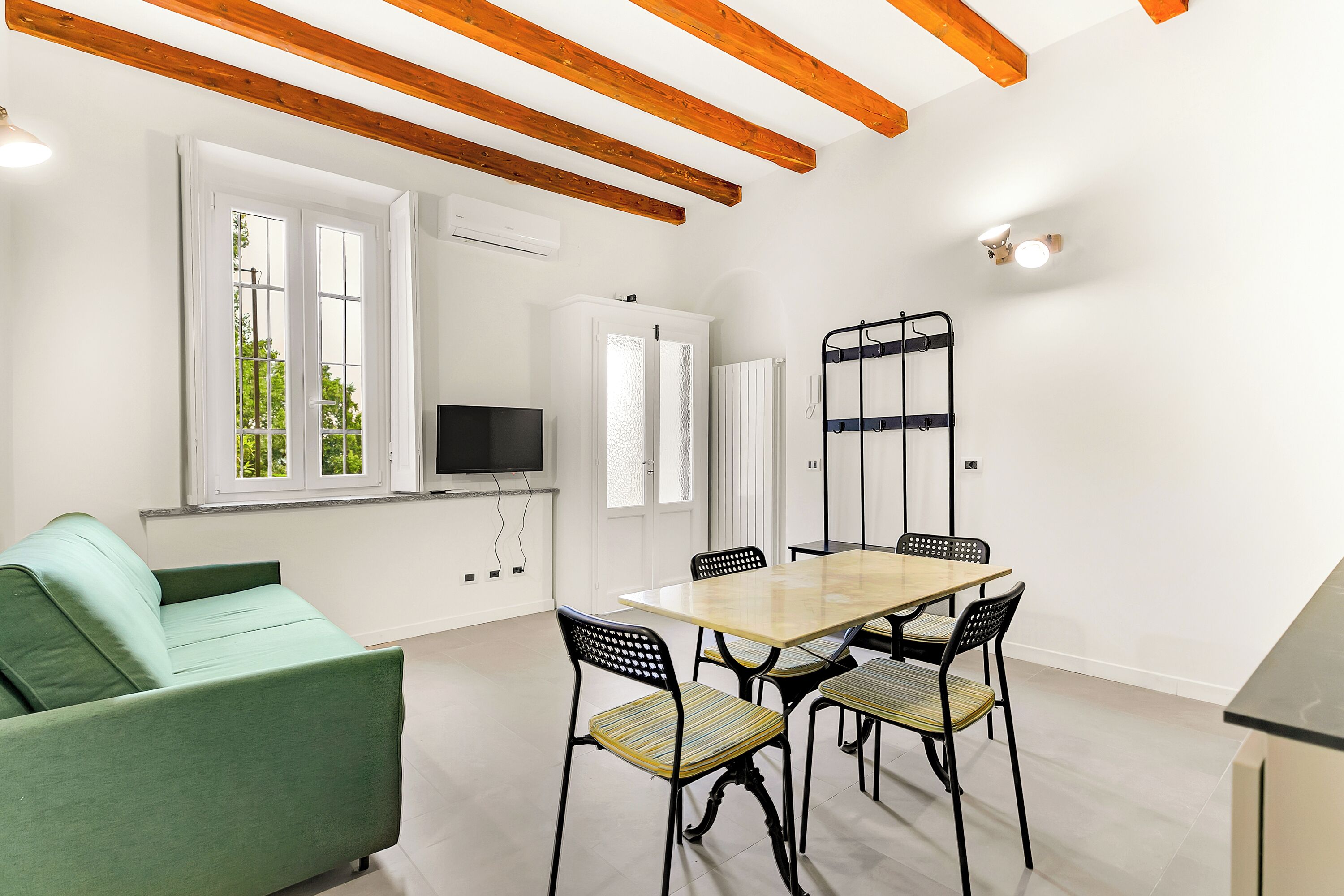 Uma sala de estar moderna com um sofá verde, uma mesa de jantar de madeira com quatro cadeiras, uma TV e um guarda-roupa.