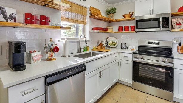 Uma cozinha moderna com armários brancos, eletrodomésticos de aço inoxidável e prateleiras de madeira.