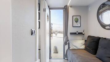 Interior compacto e moderno, com uma cama, um pequeno espaço de estar e vista para uma área externa através de uma porta.