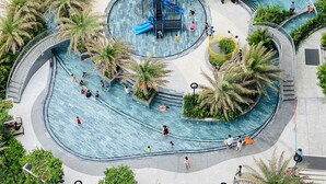 Uma piscina grande e sinuosa com várias pistas e um toboágua central, rodeada por palmeiras e vegetação.