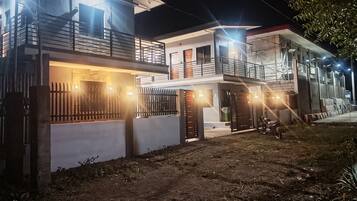 Uma casa moderna de dois andares com portão fechado, uma motocicleta estacionada na frente e uma entrada de garagem bem iluminada.