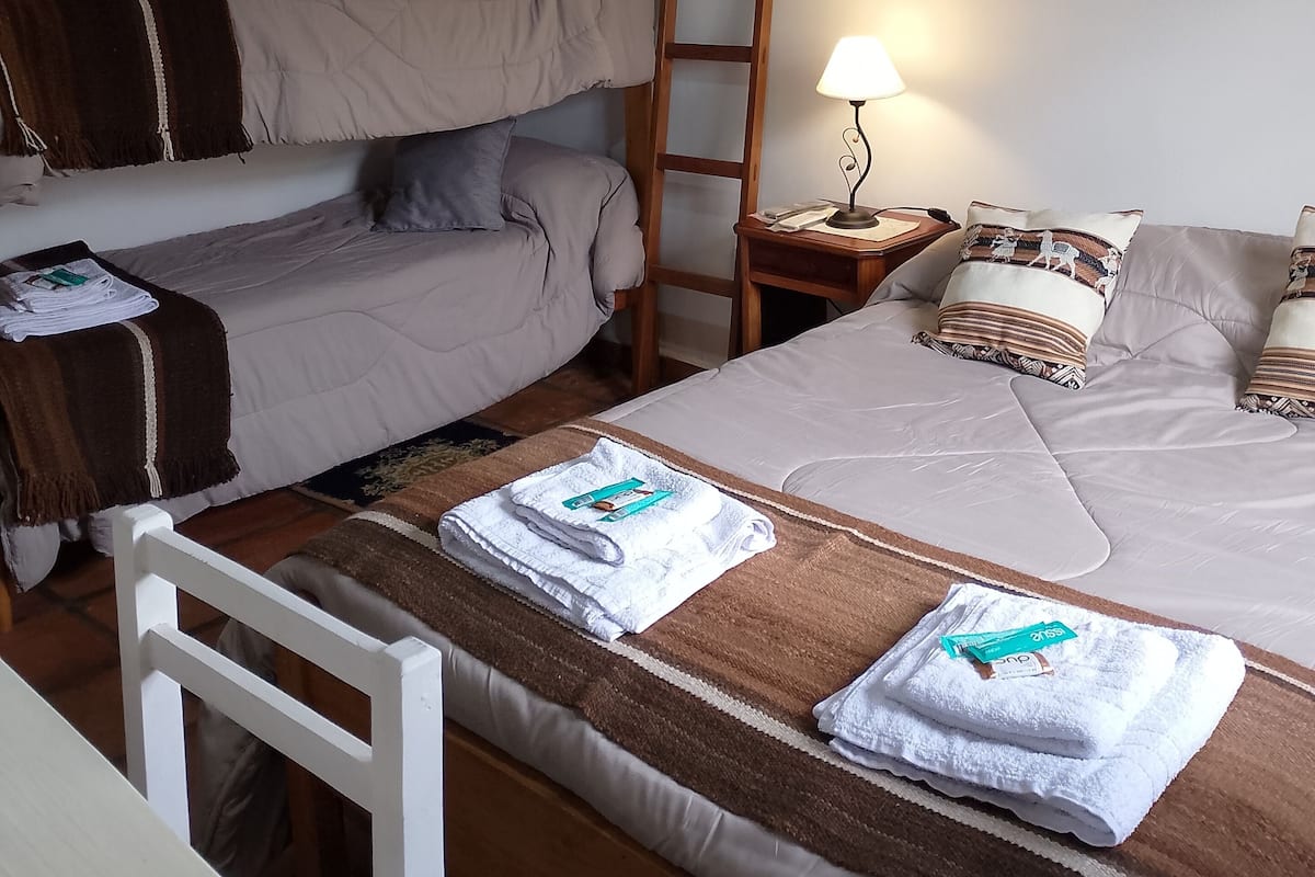 Quarto com beliches, uma mesa de cabeceira com abajur e uma prateleira pequena fixada na parede com fotos.
