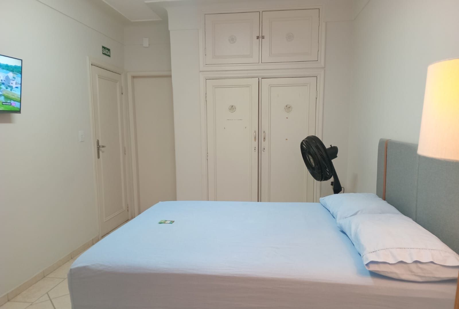 Quarto de hotel com cama, ventilador e televisão na parede.