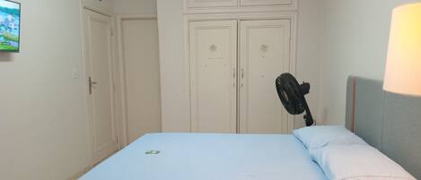 Quarto de hotel com cama, ventilador e televisão na parede.