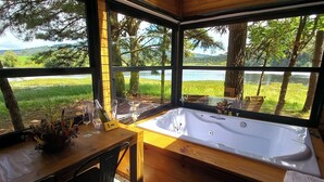 Quarto com uma banheira grande, móveis de madeira e vista para um lago e vegetação.