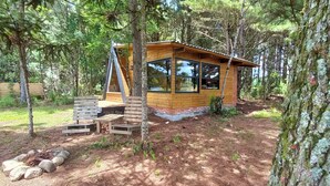 Uma cabana de madeira com uma janela grande, rodeada por árvores e uma lareira.