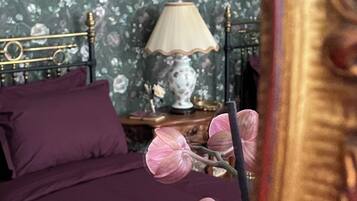 Quarto com cama, mesa de cabeceira, abajur e papel de parede floral.