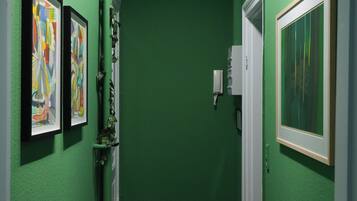 Corredor com paredes verdes, obras de arte emolduradas, uma porta branca e um acessório de iluminação.