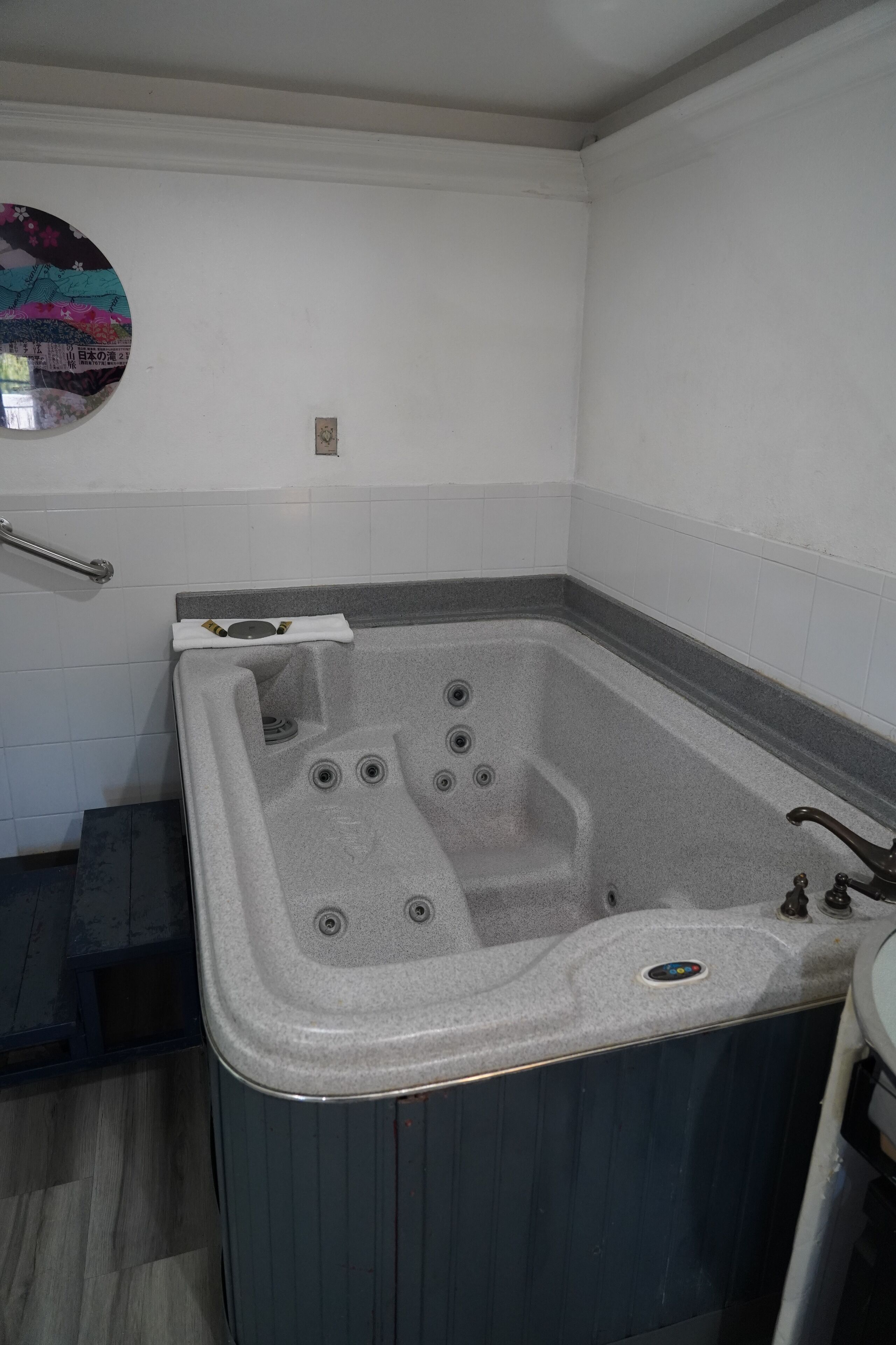 Uma banheira de hidromassagem retangular com vários jatos, um porta-toalhas e um pequeno degrau para entrar.