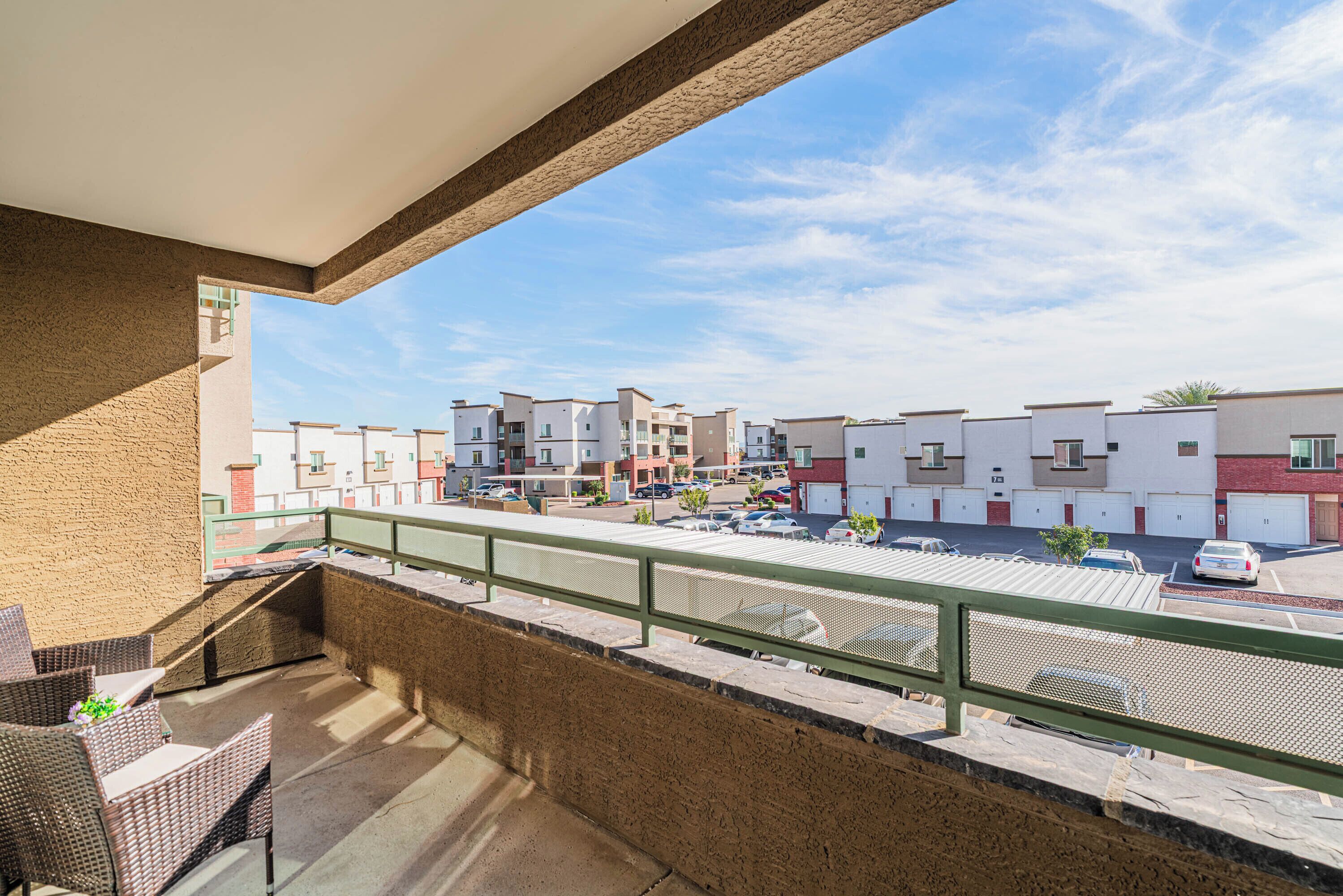 Uma varanda com móveis de vime, vista para um estacionamento e edifícios altos ao fundo.