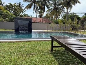 Piscina com cascata, cercada por grama e palmeiras.