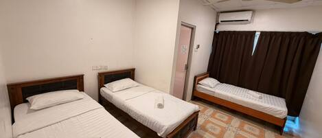 Quarto de hotel com três camas de solteiro, ventilador de teto, aparelho de ar condicionado e piso estampado.