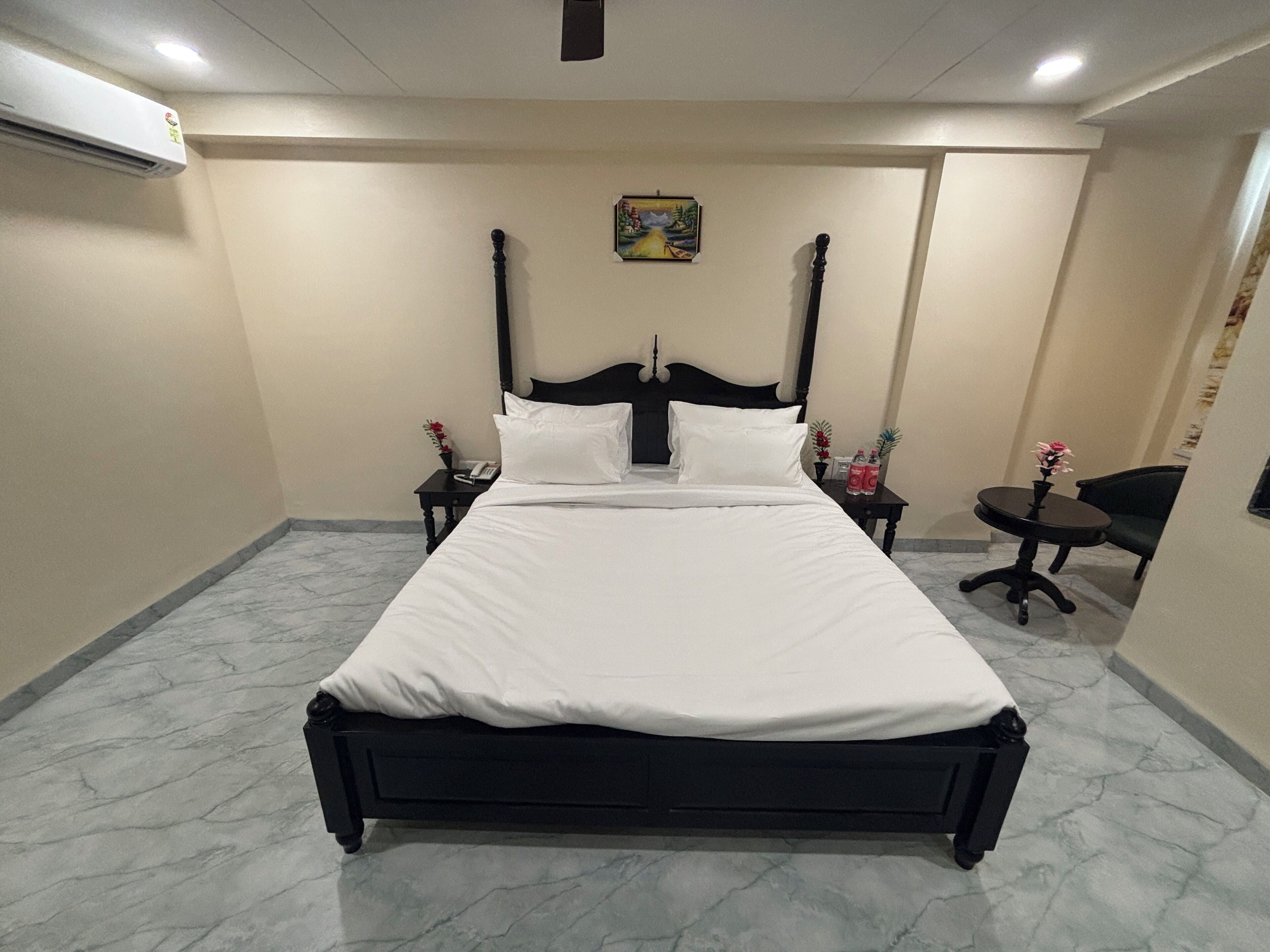 Cama bem arrumada com lençóis brancos, cabeceira preta e uma pequena mesa de cabeceira com um telefone e uma garrafa.