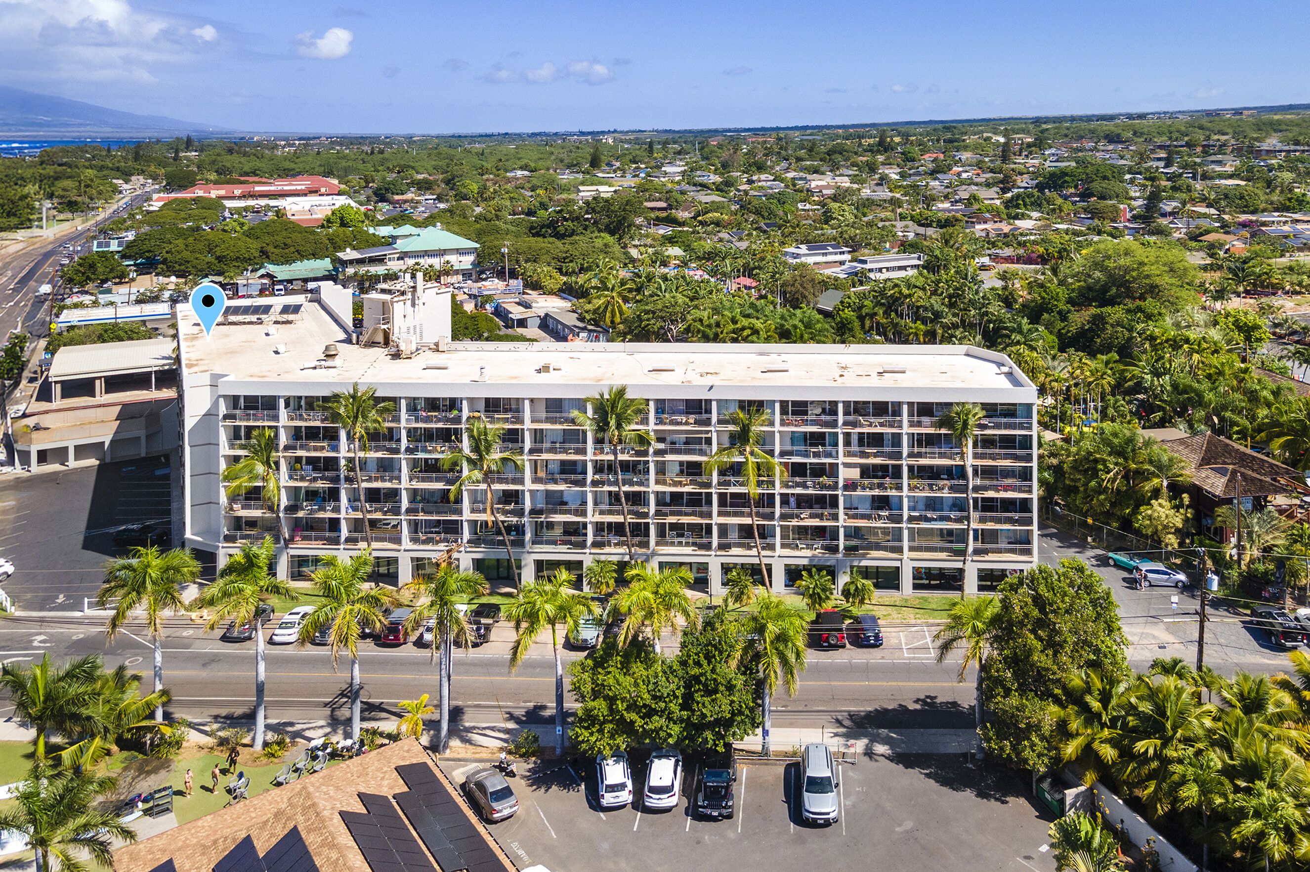 Um hotel com vários andares e design moderno, com um estacionamento com vários carros e palmeiras.