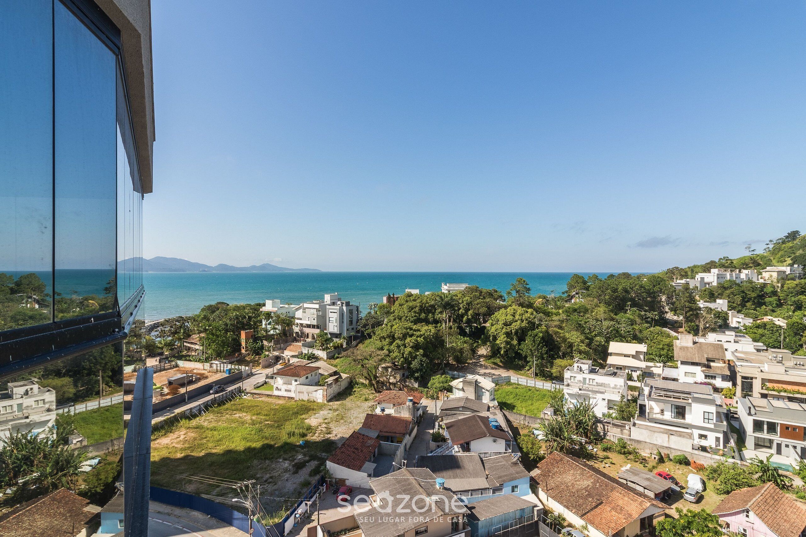 Zona residencial costeira com casas, céu claro e o oceano ao fundo.