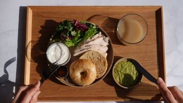 Uma bandeja de madeira com uma salada, fatias de peru, um bagel e duas tigelas de molho.