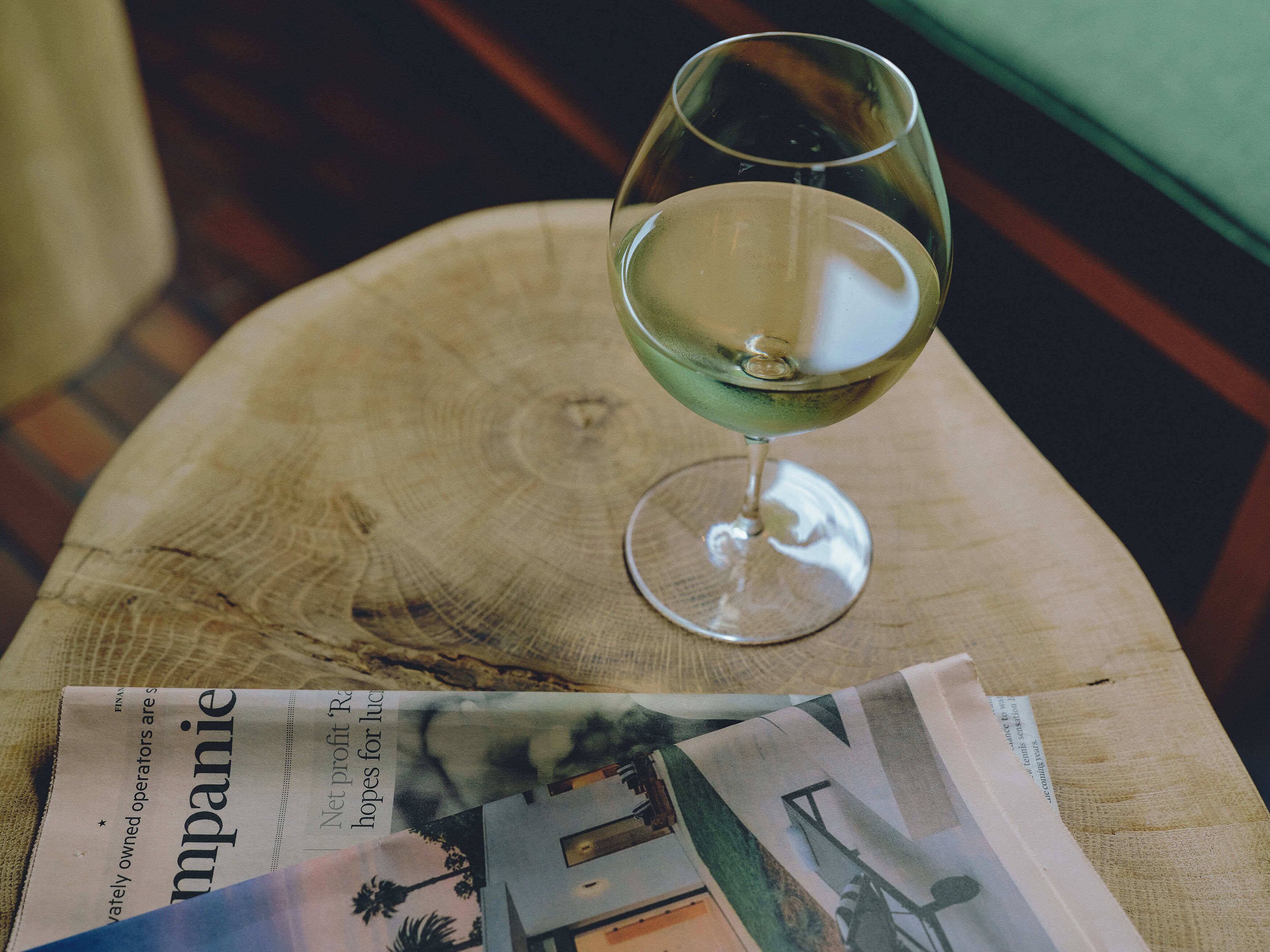 Um copo de vinho branco sobre uma mesa de madeira com um jornal.