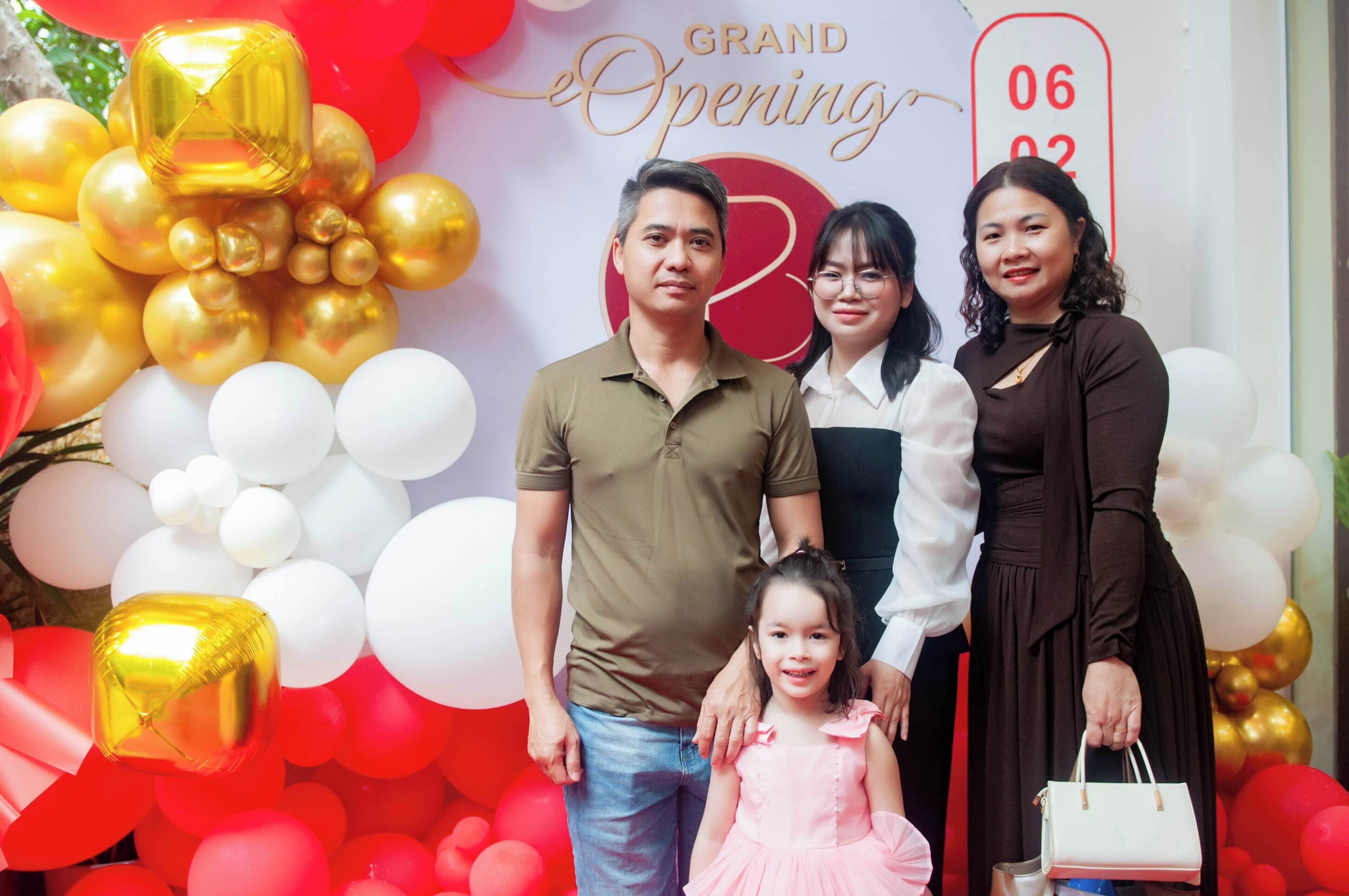 Uma família posando em frente a um painel com o texto 'GRAND Opening' e balões.