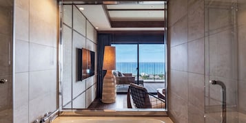 Uma casa de banho moderna com cabine de duche em vidro, banheira e vista para uma varanda com mobiliário exterior.