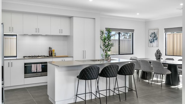 Uma cozinha moderna com armários brancos, uma ilha central com banquetas, uma área de refeições com mesa redonda e uma grande janela que oferece luz natural.