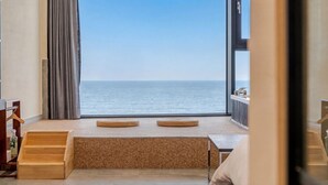 Quarto com vista para o mar, um banco de madeira, uma mesinha e um radiador.