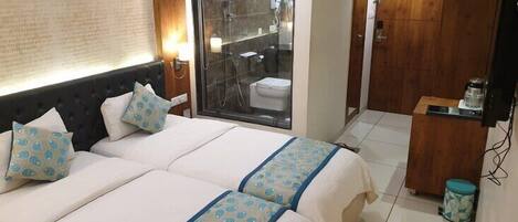 Quarto de hotel com uma cama, banheiro com box de vidro e armário de madeira.