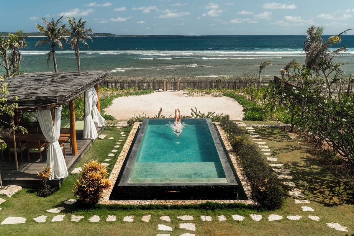Piscina com vista para o oceano, rodeada por um deck e palmeiras.