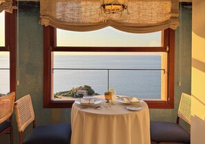 Mesa posta para dois, com vista para o mar através de uma grande janela.