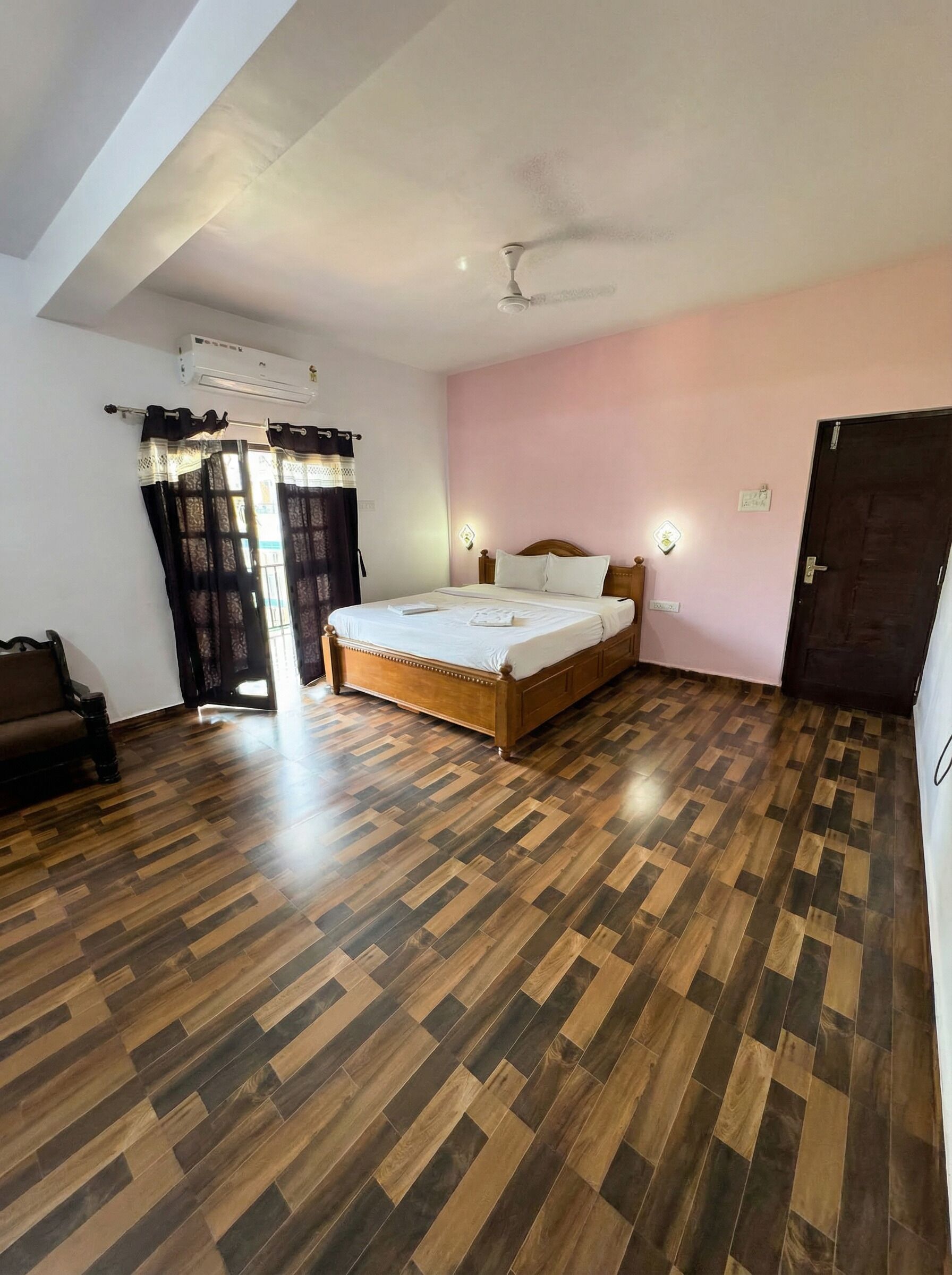 Um quarto com piso de madeira, uma cama com encosto e um ventilador de teto, além de uma porta.