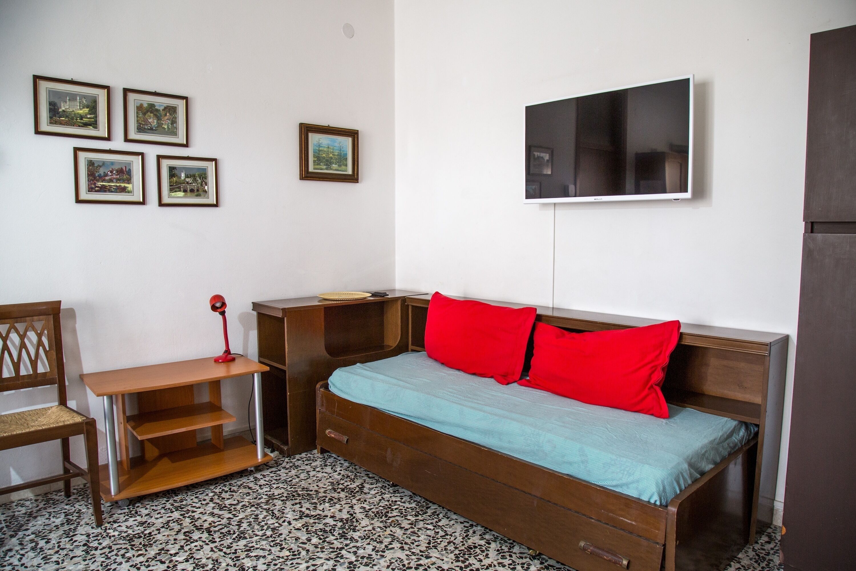 Quarto compacto com cama, escrivaninha, cadeira e TV fixada na parede.