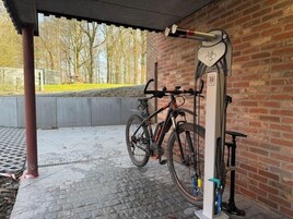 Uma área de estacionamento coberta para bicicletas, com muro de tijolos e suporte metálico.