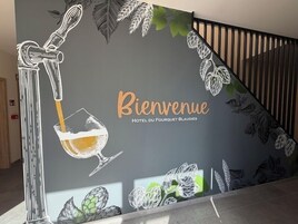 Paredes com um letreiro 'Bienvenue', ilustração de uma taça de vinho e desenhos de videiras.