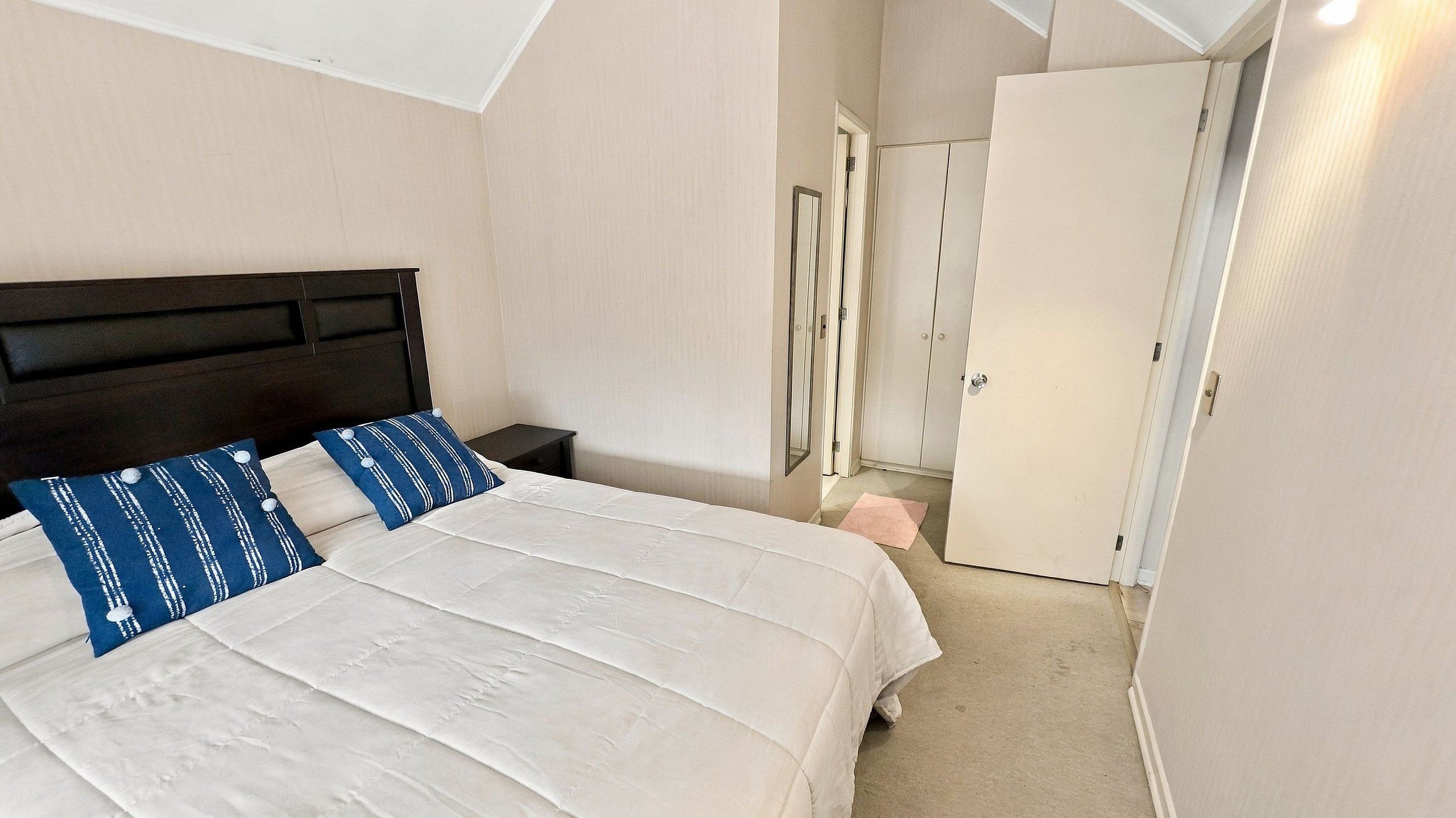 Quarto com cama, mesa de cabeceira, guarda-roupa e porta.
