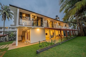 Uma casa moderna de dois andares com varanda, um gramado bem cuidado e um muro de pedra.