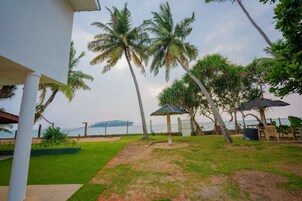 Uma área externa coberta com vista para o mar, palmeiras e um pequeno espaço de estar com mesa e cadeiras.