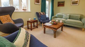 Uma sala de estar com um sofá verde, uma poltrona azul e uma mesa de centro de madeira com uma fruteira.