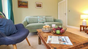 Sala de estar com um sofá verde, uma mesa de centro de madeira com revistas e uma fruteira.