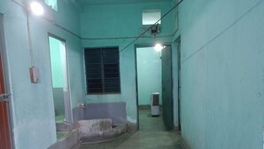 Um corredor estreito com piso de concreto, uma janela com barras de metal e um quadro de eletricidade fixado na parede.