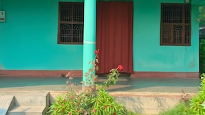 Um edifício com fachada azul-esverdeada, uma porta vermelha e duas janelas com grades de metal.