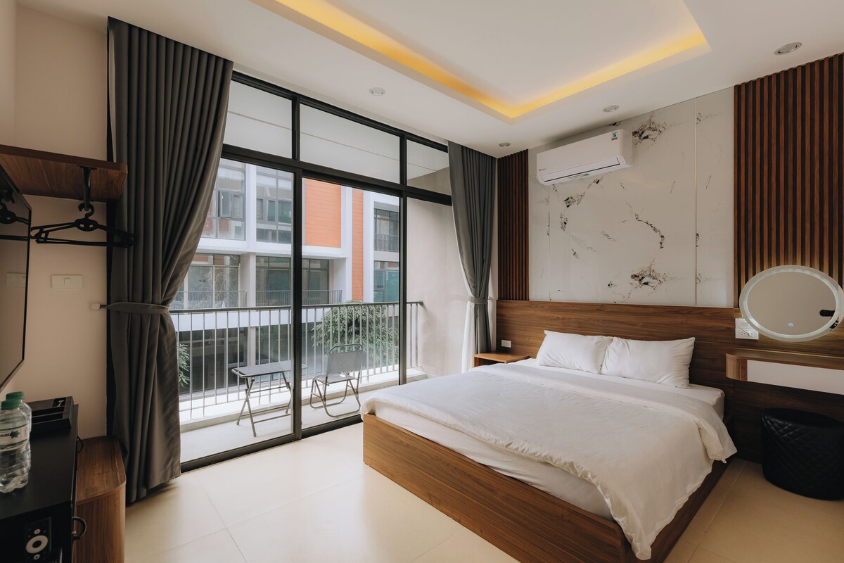Quarto de hotel com uma cama grande, mesa de cabeceira com espelho, vista para a varanda exterior e um design moderno no teto.