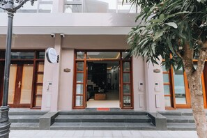 Entrada de hotel com placa, escadaria e uma grande planta em vaso.