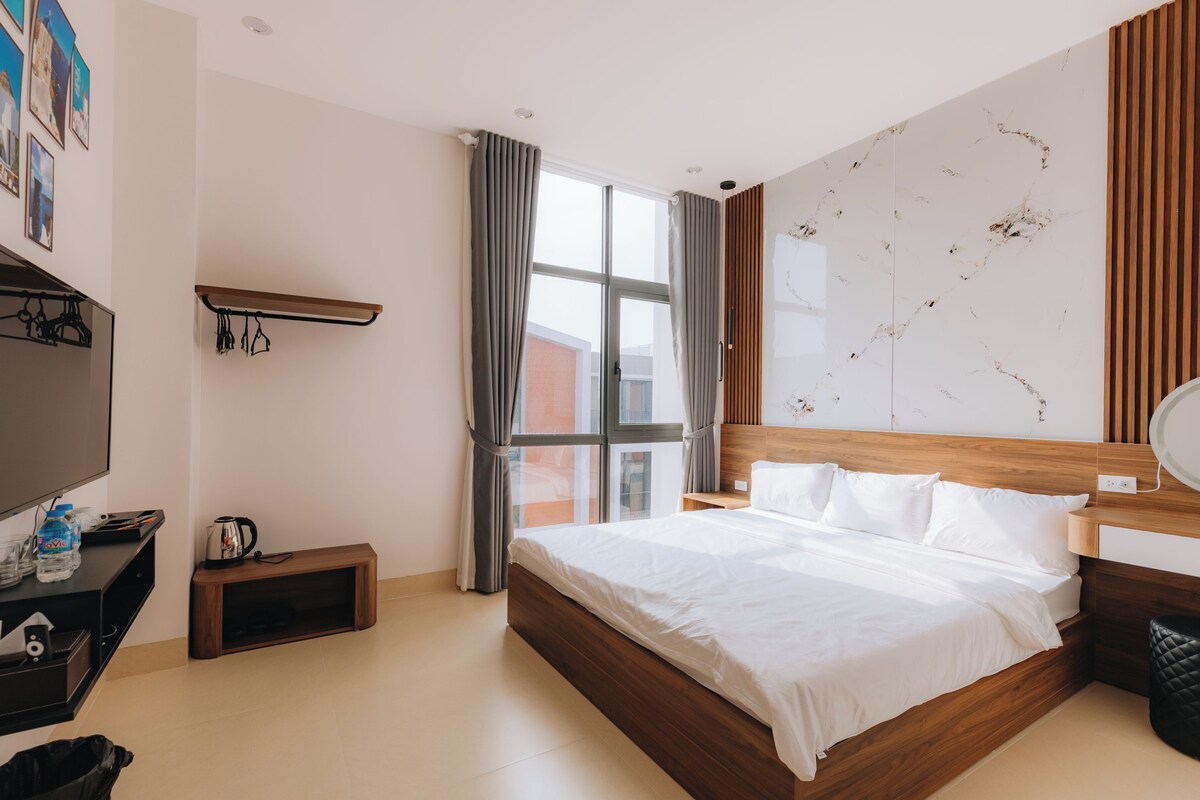 Quarto de hotel com cama, televisão, cafeteira e janela com cortinas.