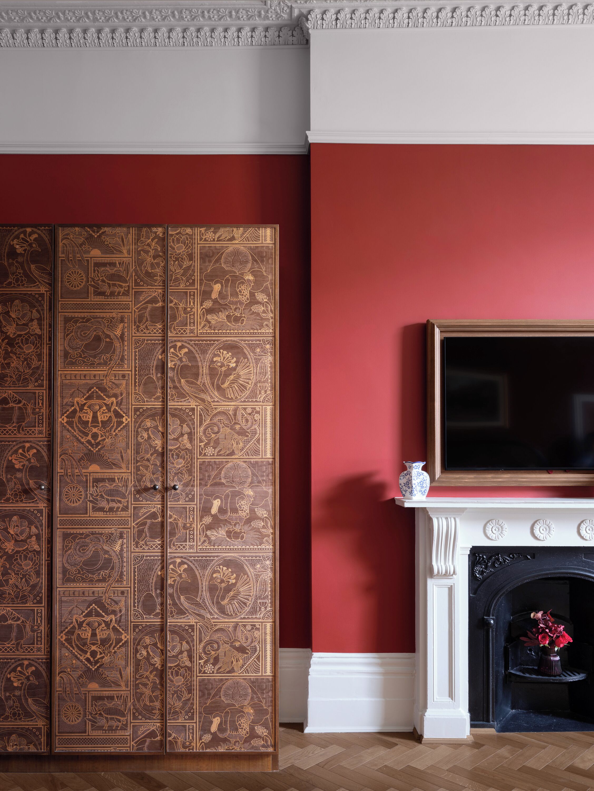 Um quarto com uma parede vermelha, uma lareira branca e um armário de madeira com esculturas detalhadas.