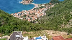 Vista aérea de uma cidade costeira com um edifício central que possui um estacionamento e um terraço com painéis solares.