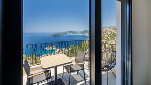 Uma varanda com mesa e cadeiras, com vista para a paisagem costeira, montanhas e o mar.