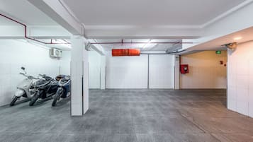 Espaço interno limpo e bem iluminado, com piso de azulejos, teto com canos e um ventilador visíveis, e uma placa de saída de emergência vermelha.