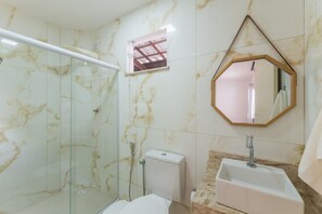 Uma casa de banho com cabine de duche em vidro, sanita, lavatório e espelho na parede.