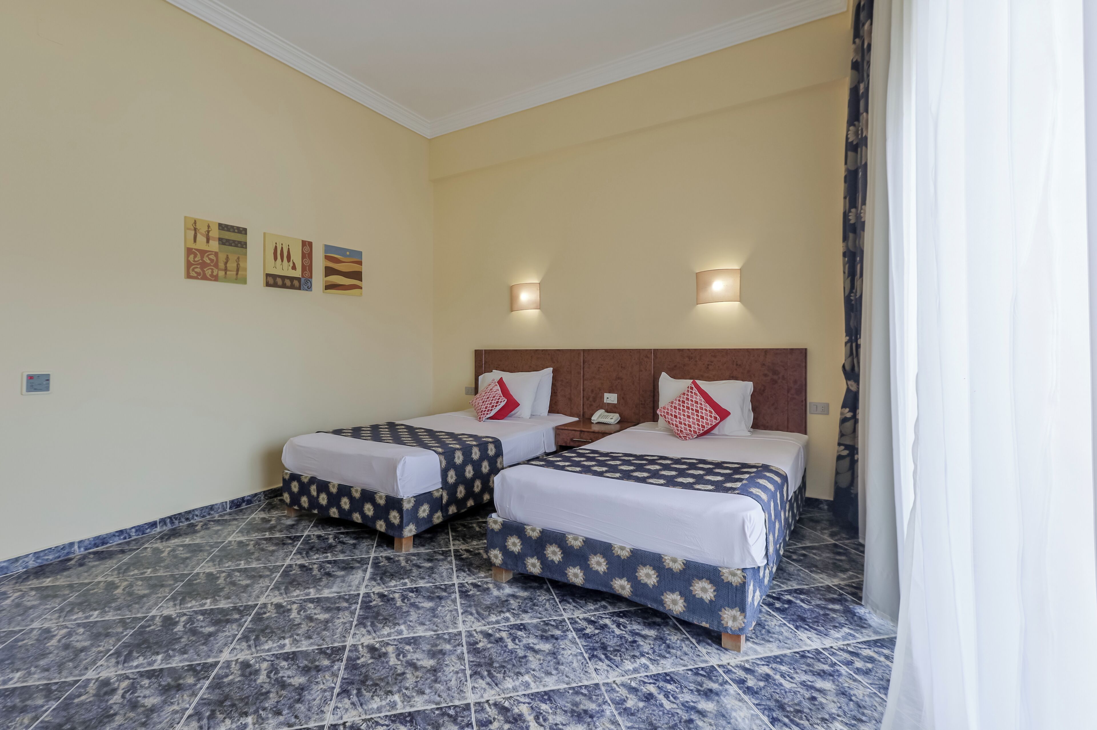 Quarto de hotel com duas camas, piso de mármore e luminárias fixadas na parede.